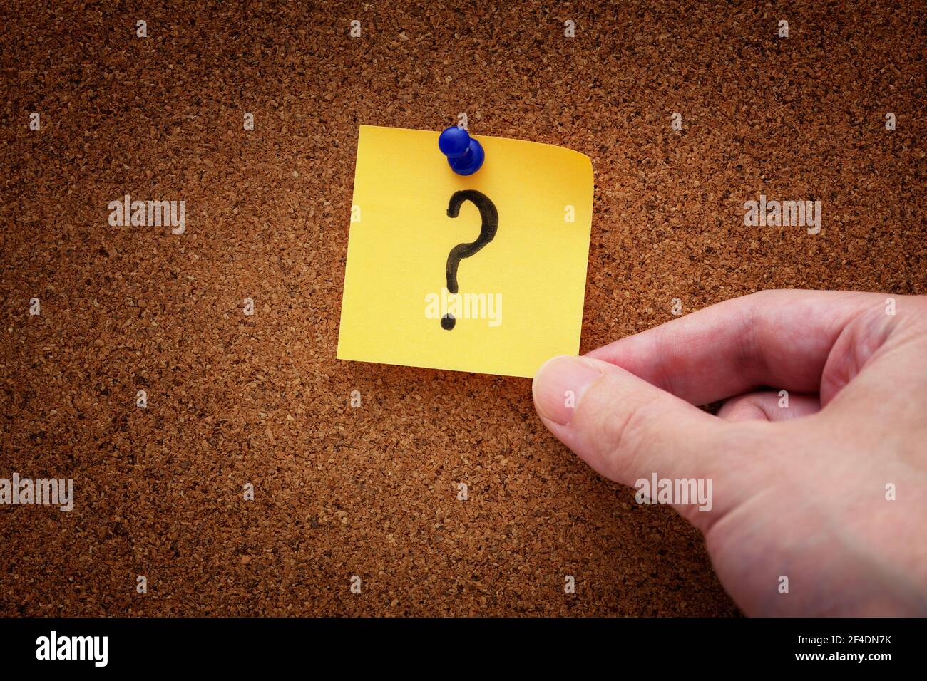 A man taking a pinned paper note with a question mark from a cork board ...