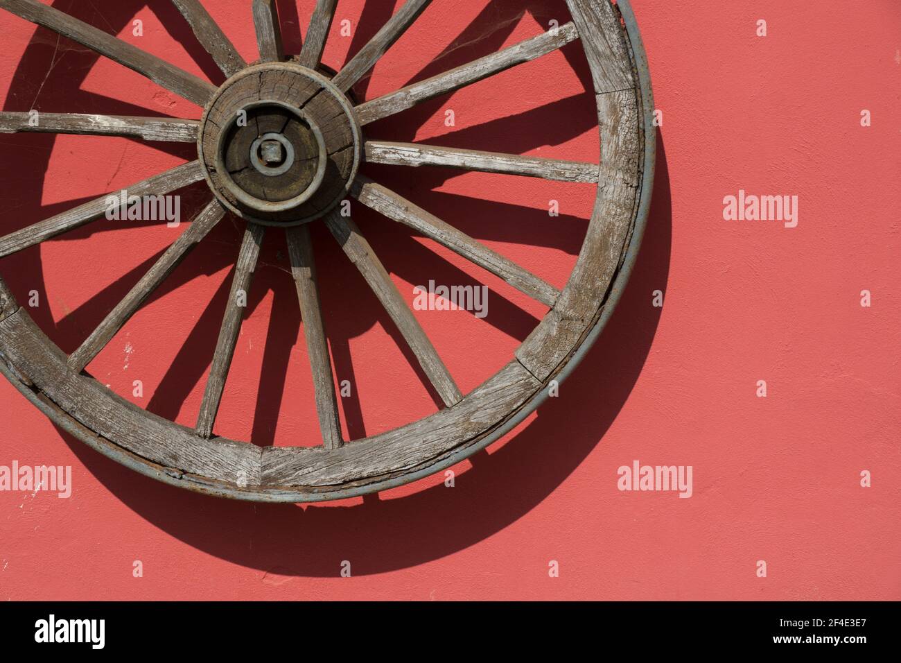 old carriage wheel hanging on a red wall with diagonally marked shadows ...