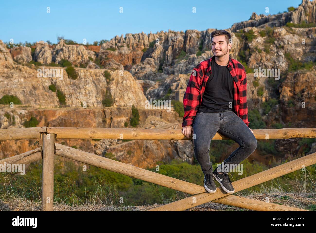 A handsome young Spanish man sitting on the log railing and smiling on ...
