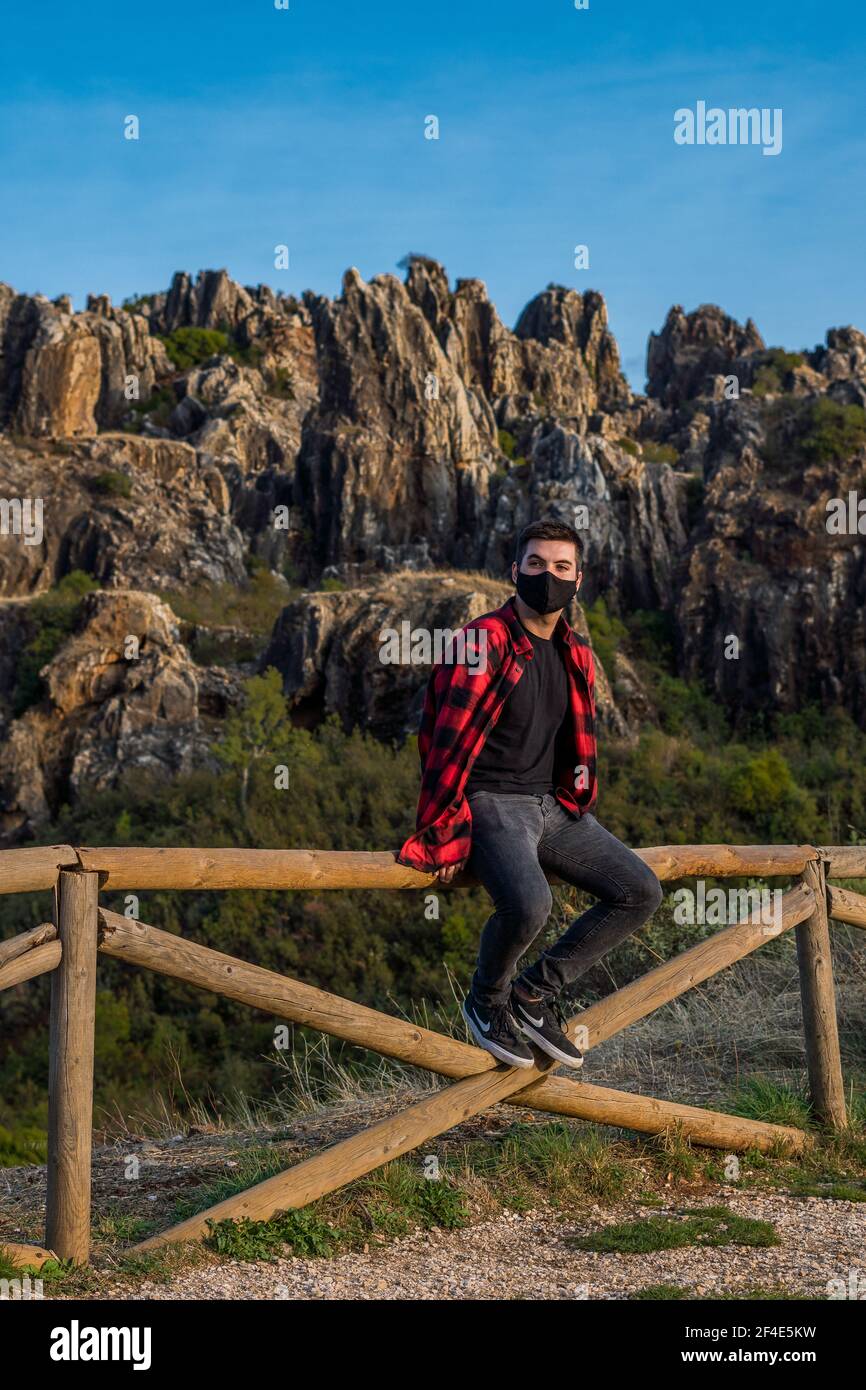 A vertical shot of a young Spanish man wearing a mask and sitting on a ...