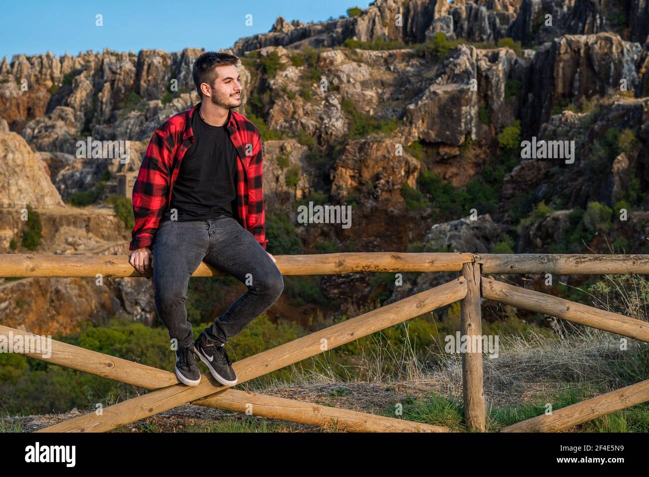 A handsome young Spanish man sitting on the log railing and smiling on ...