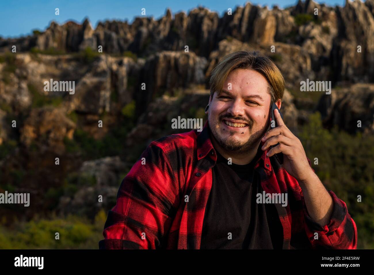 A young Spanish man talking on the phone on a background of a rocky ...