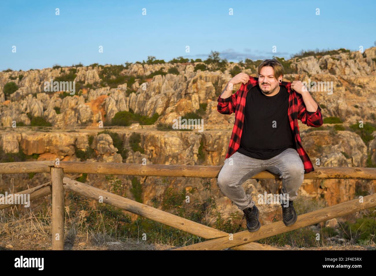 A young Spanish man sitting on a log railing and smiling on a ...
