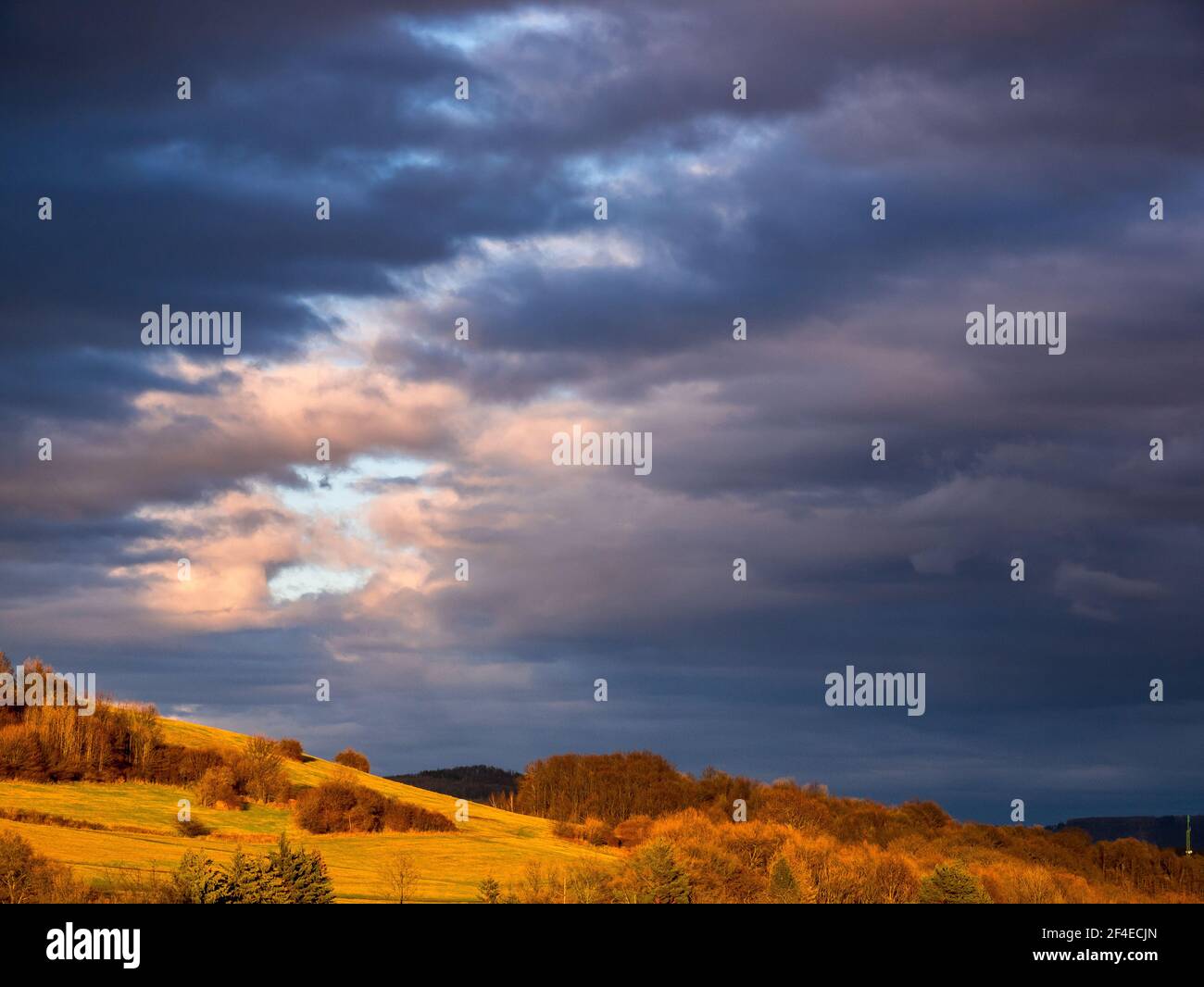 A rift in dense clouds in the sky above a hill in the evening lit by ...
