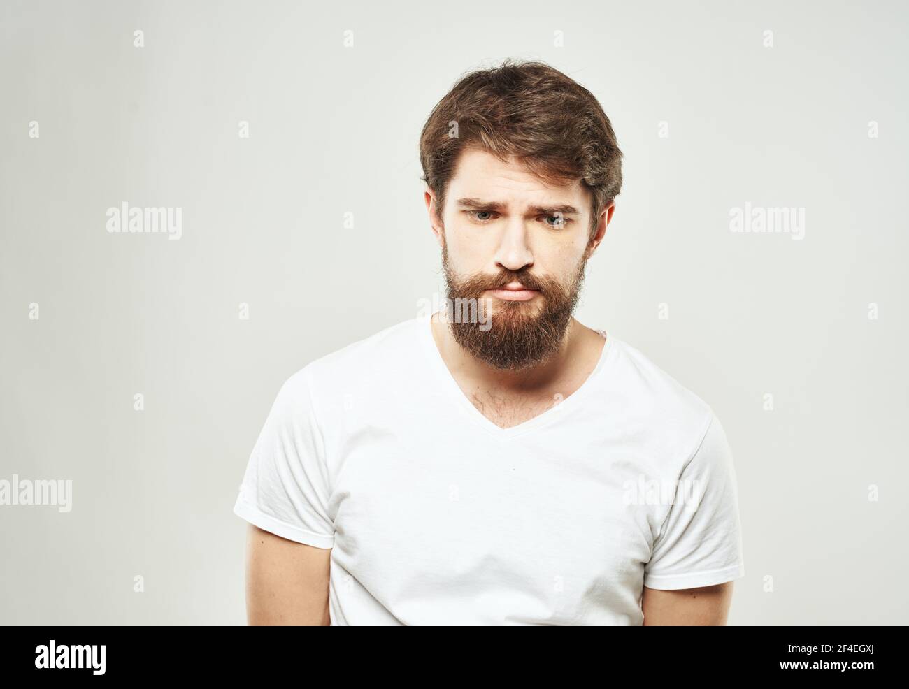 Guy in a white T-shirt on a light background emotions sad face cropped ...