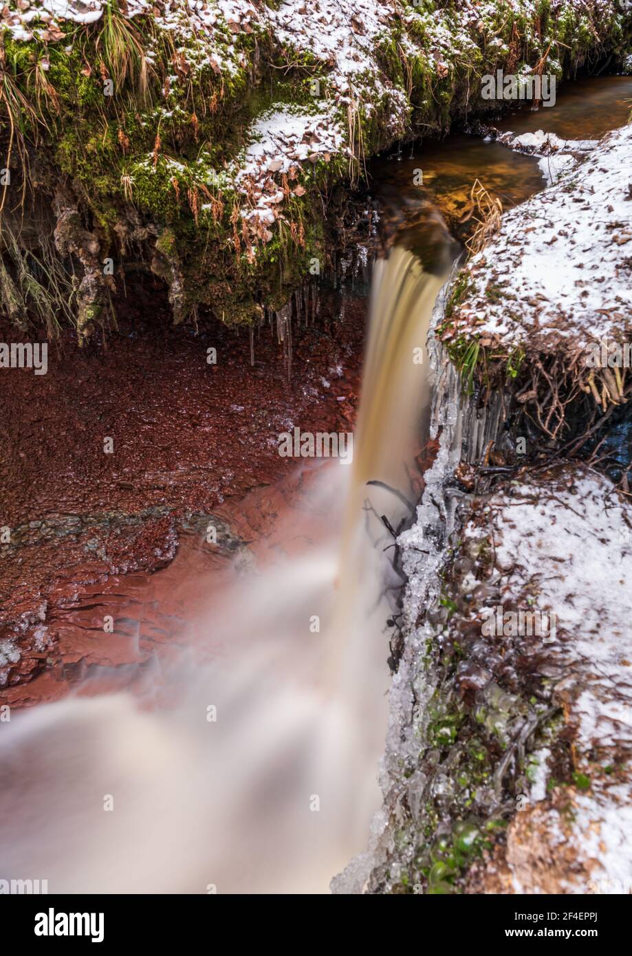 small river waterfall in the forest with a thin layer of snow on the ...