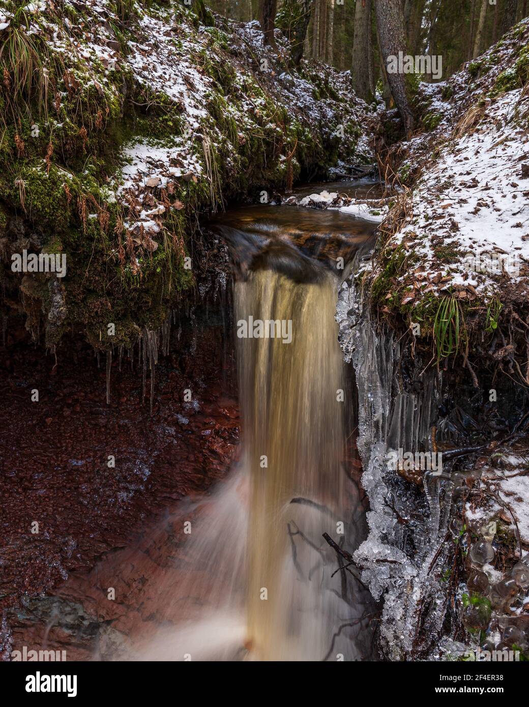 small river waterfall in the forest with a thin layer of snow on the ...