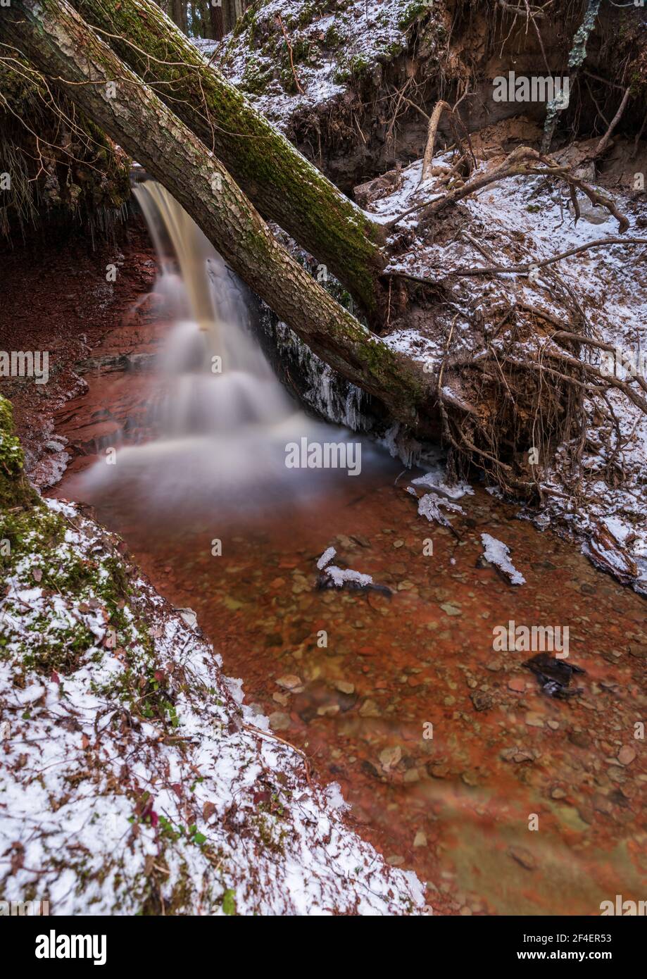 small river waterfall in the forest with a thin layer of snow on the ...