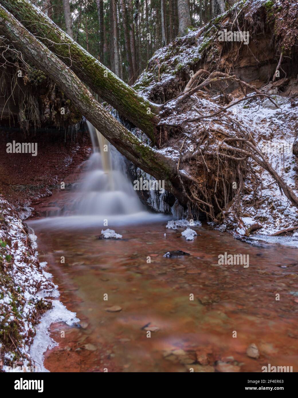 small river waterfall in the forest with a thin layer of snow on the ...