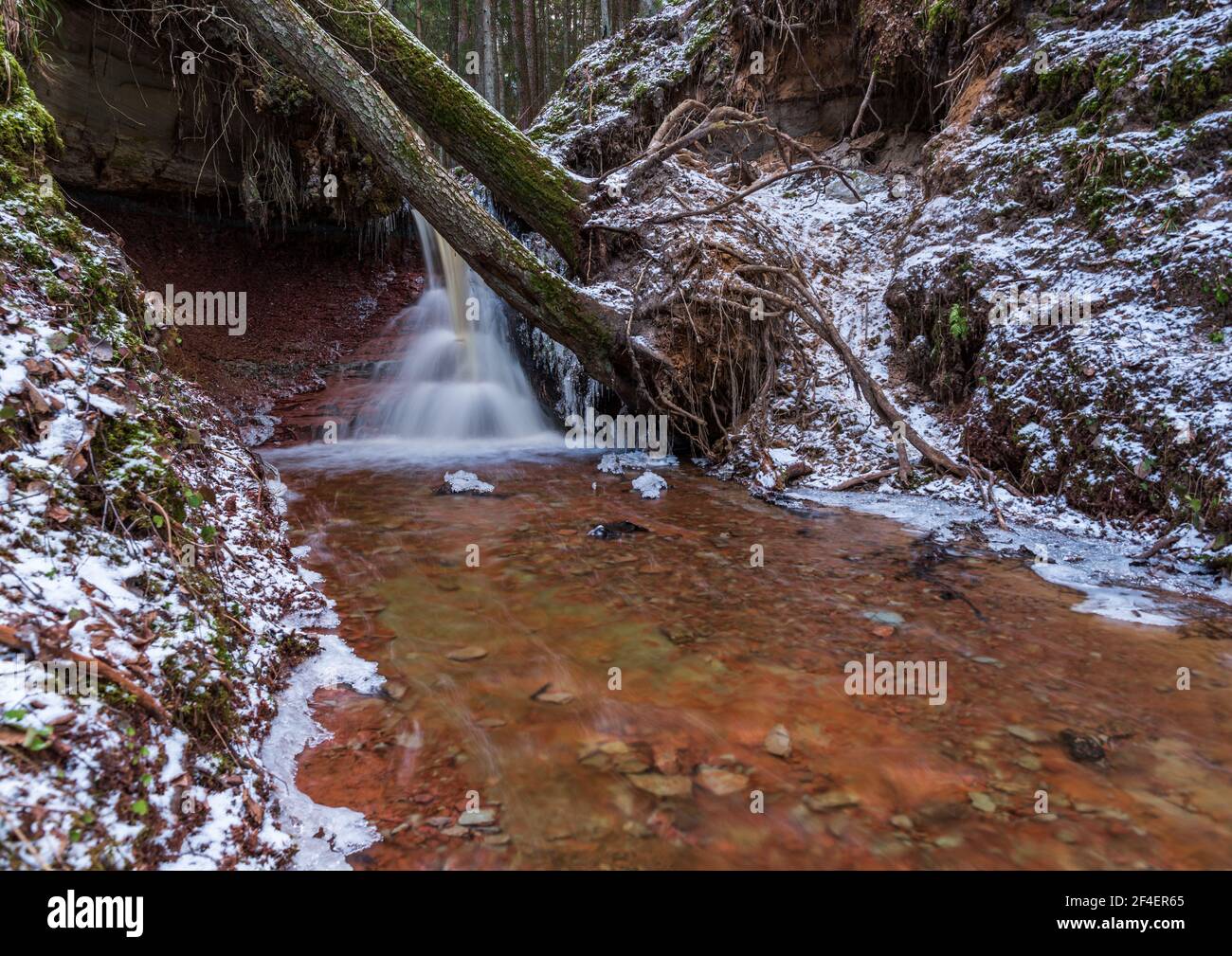small river waterfall in the forest with a thin layer of snow on the ...