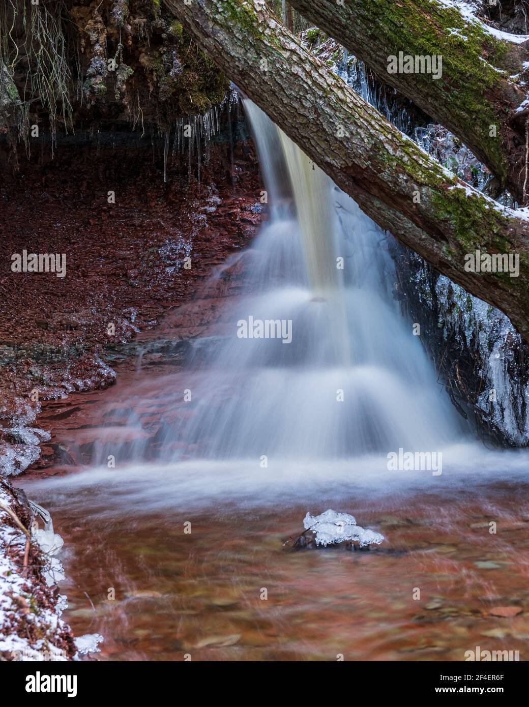 small river waterfall in the forest with a thin layer of snow on the ...