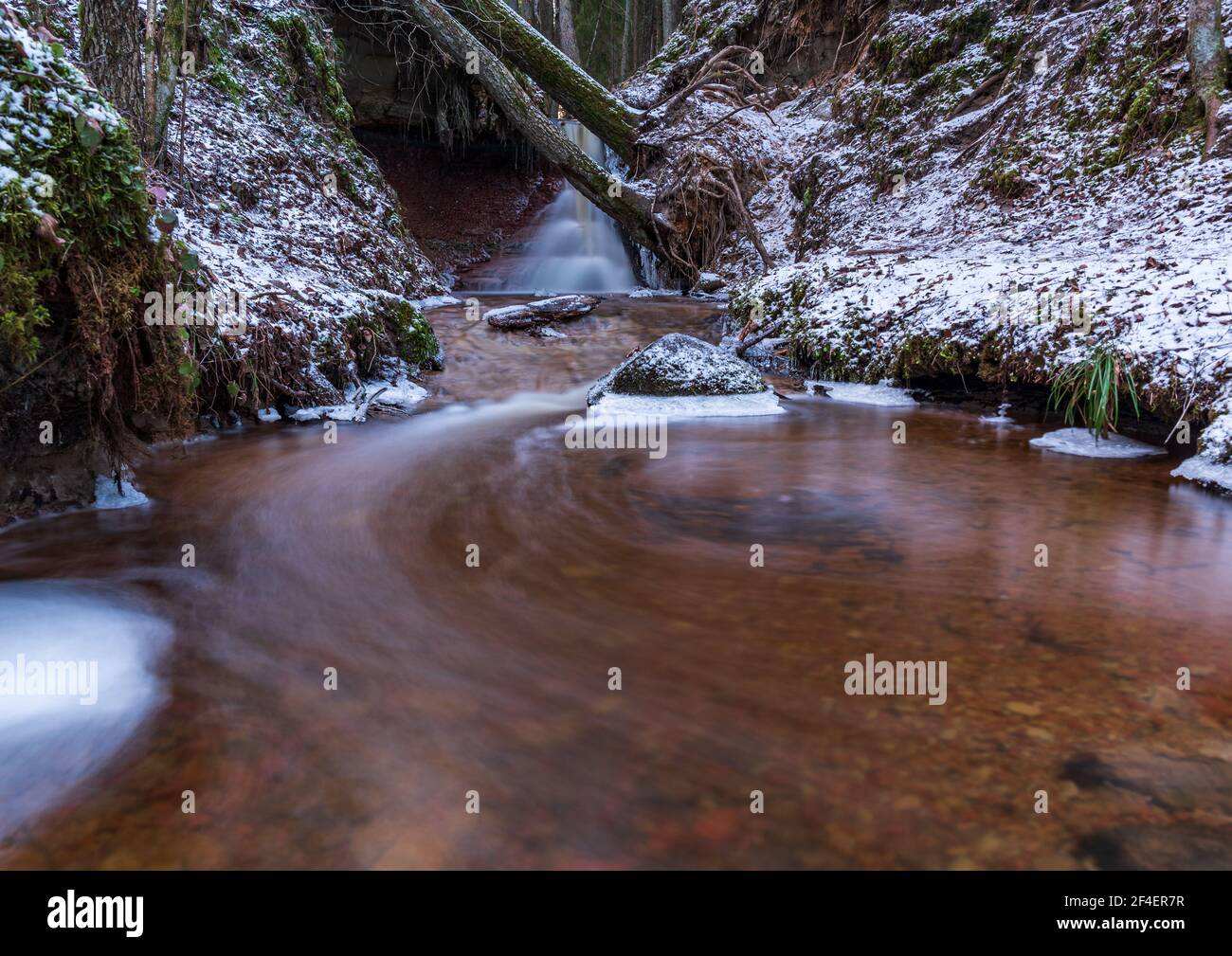 small river waterfall in the forest with a thin layer of snow on the ...