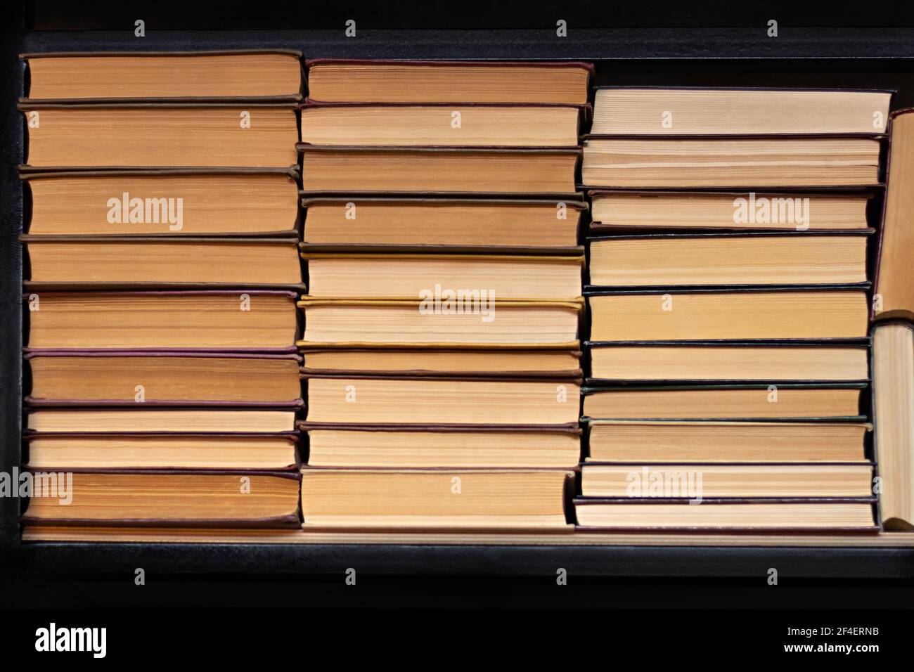 Stacks of old books rows lie on a bookshelf close-up. Many books stand ...