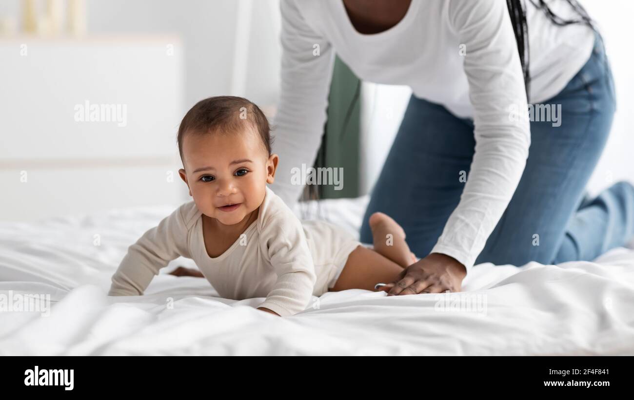 Cute little African American baby crawling in bed with mum Stock Photo ...