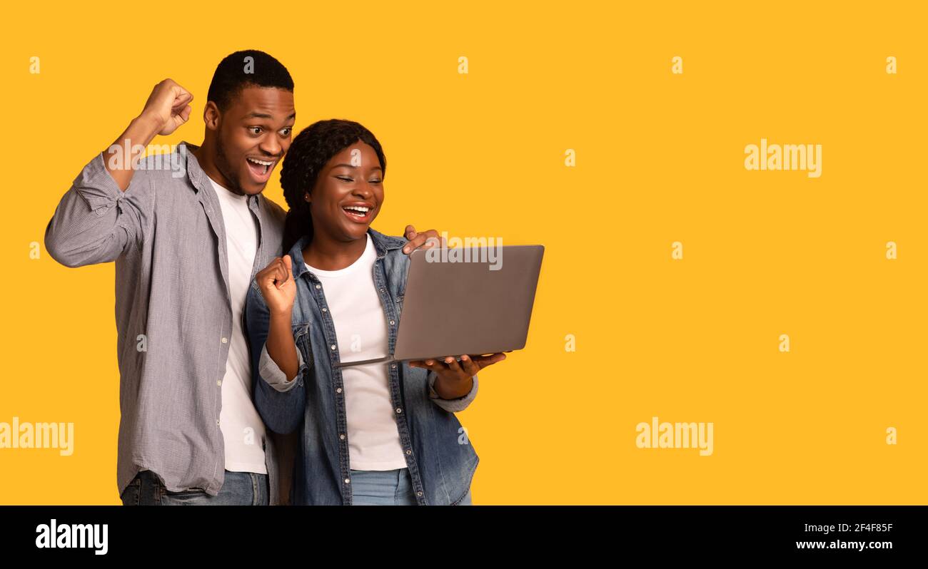 Overjoyed Black Couple Holding Laptop Computer And Raising Fists With ...