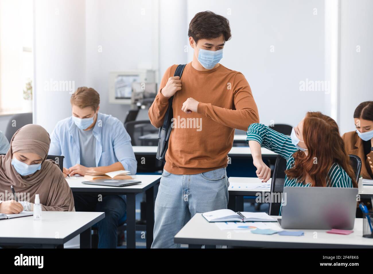 Diverse students wearing face masks greeting and bumping elbows Stock ...