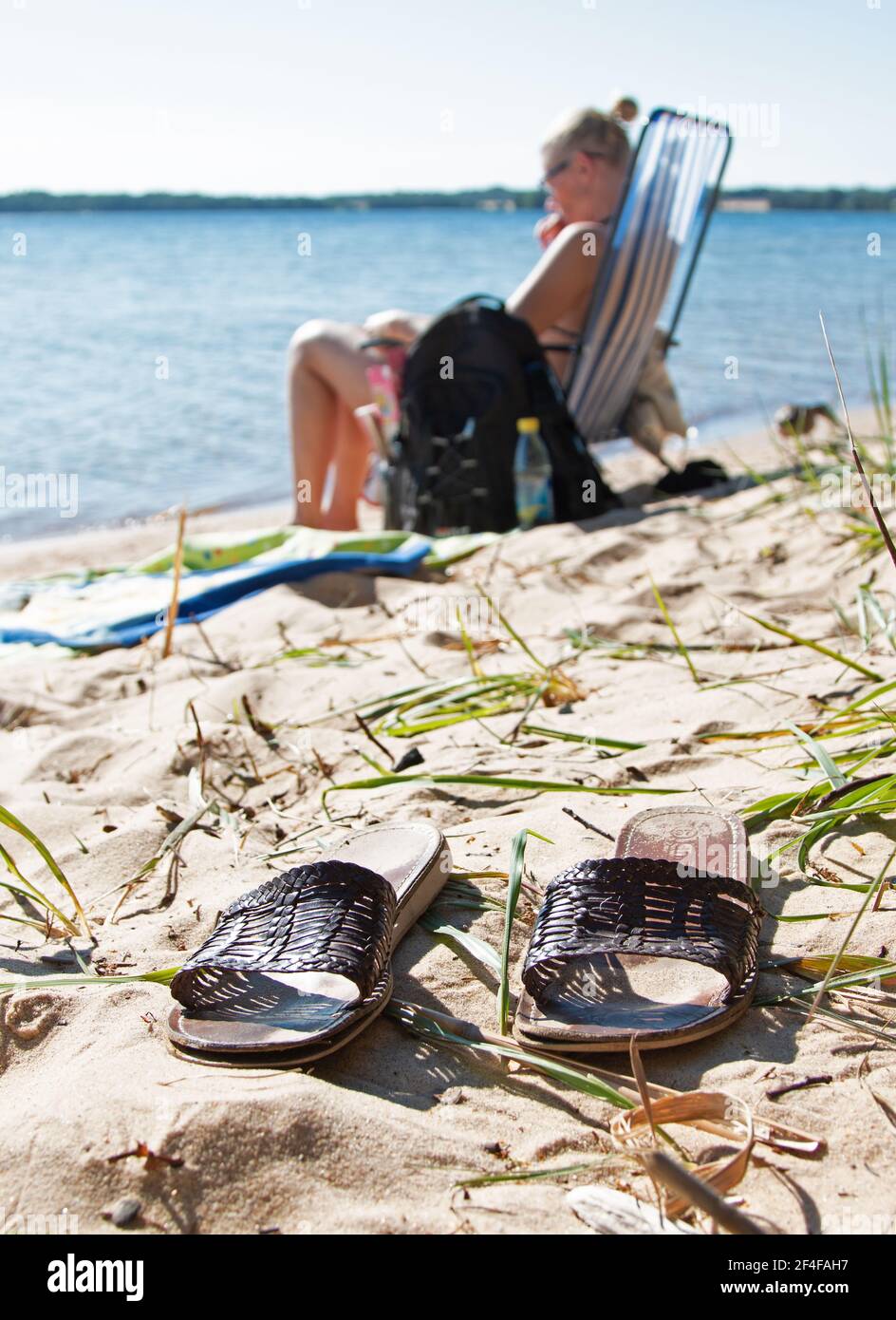A woman sitting in a deck chair reading a book on the sandy beach on a ...