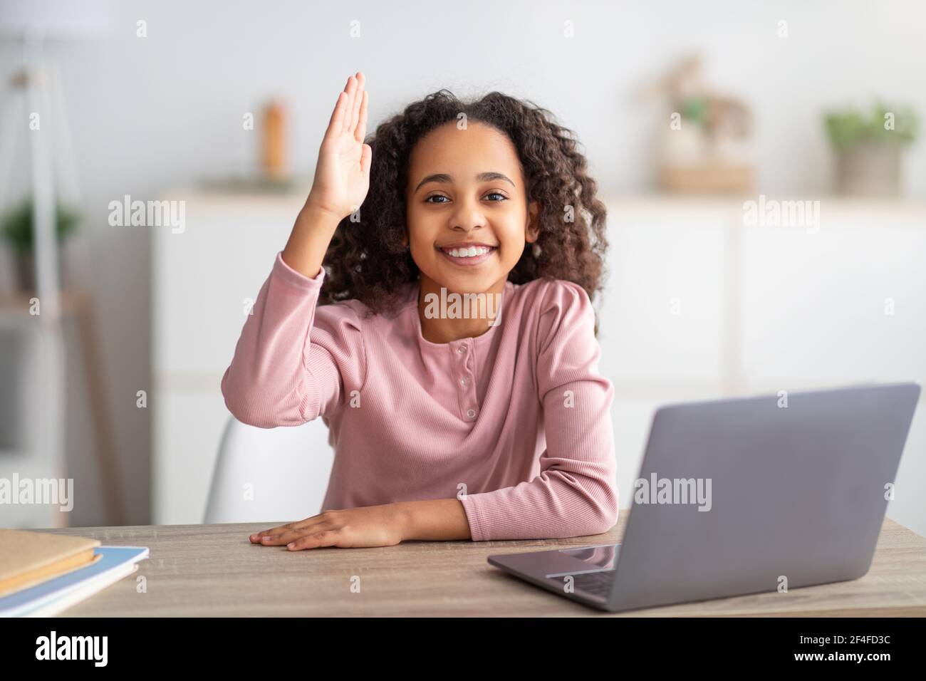 Distant education. Black schoolgirl at laptop raising hand during ...