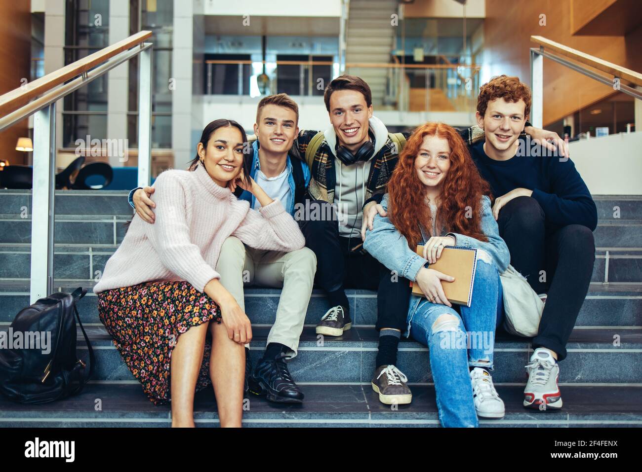 Portrait of college students sitting on stairs smiling at camera. Happy ...