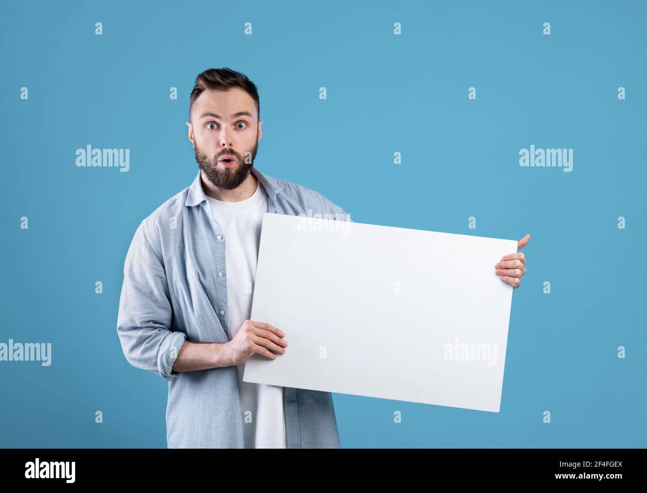 Surprised young man showing blank white poster, presenting something on ...