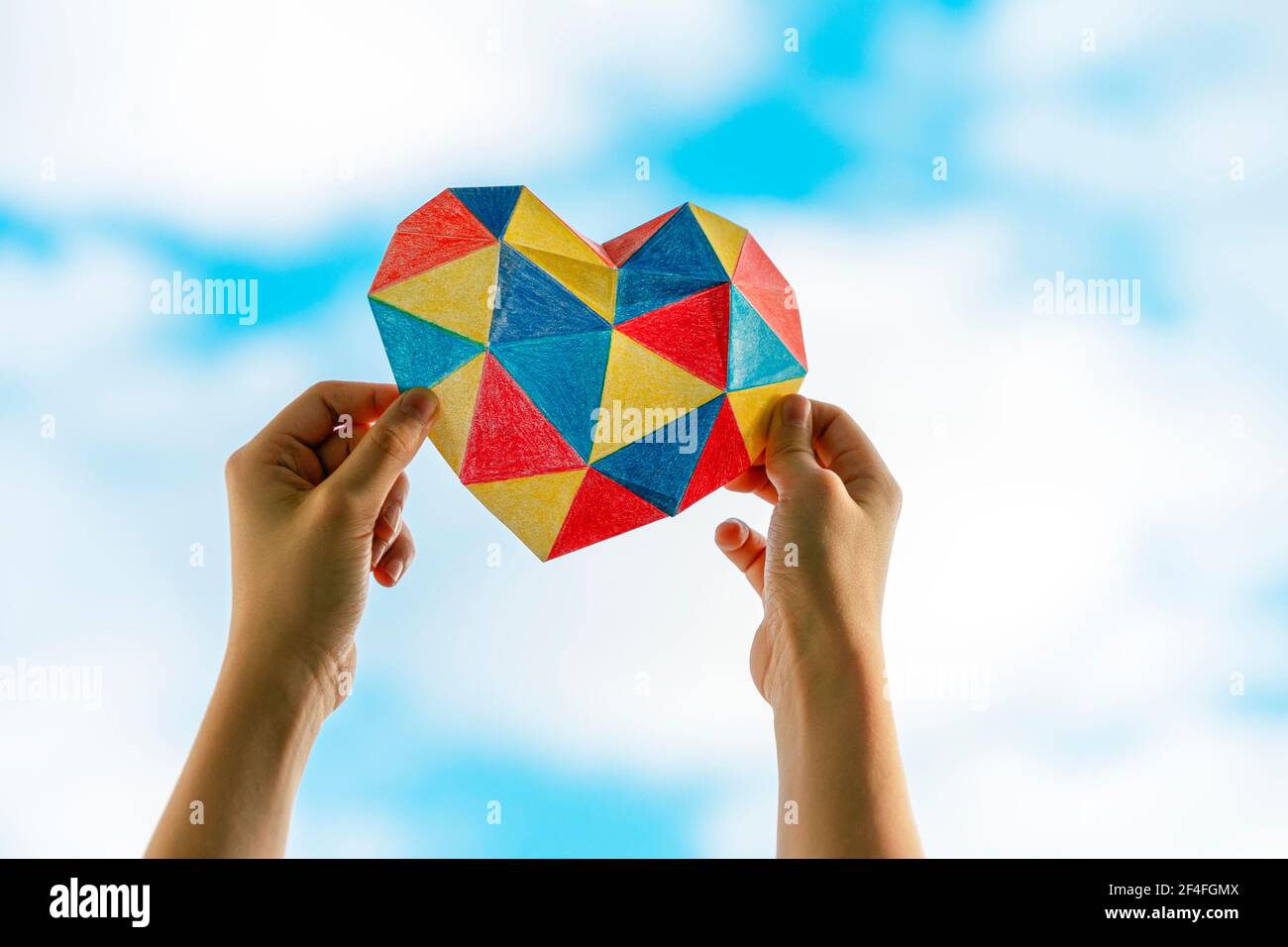 Child hands holding colorful heart over blue sky background. World ...