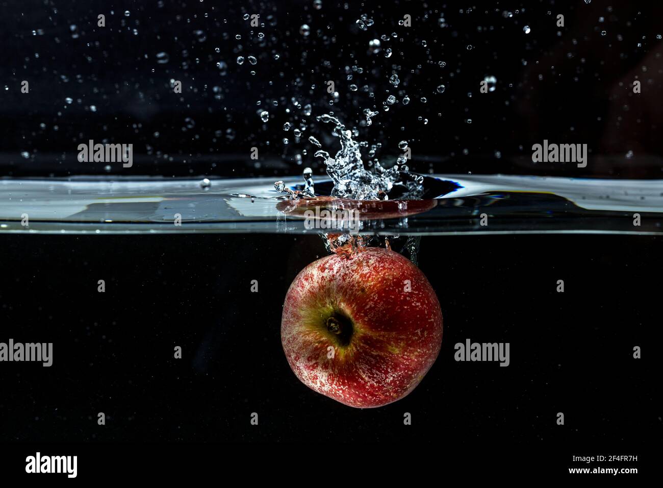 Close up view of colorful apple falling in water on black background ...
