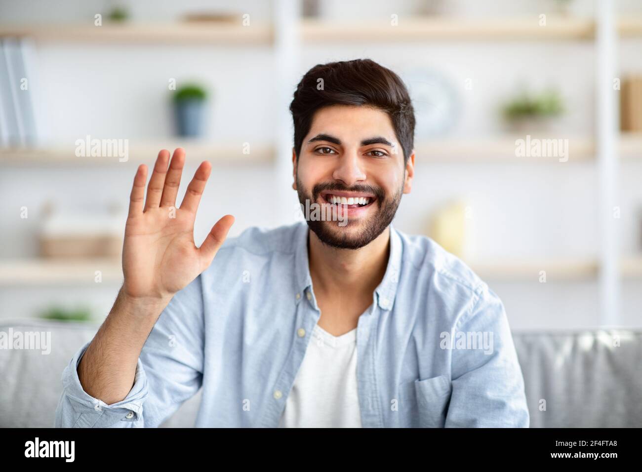 Greeting gesture concept. Happy arab man waving hand to camera, saying ...