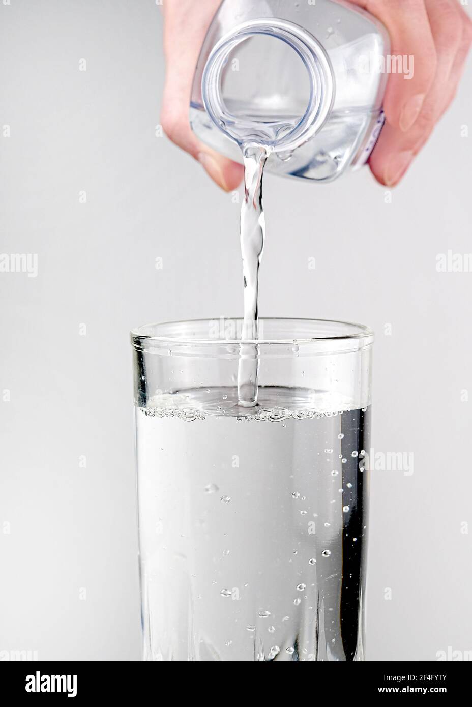 Pouring water from a bottle on glass on a light background. Natural ...