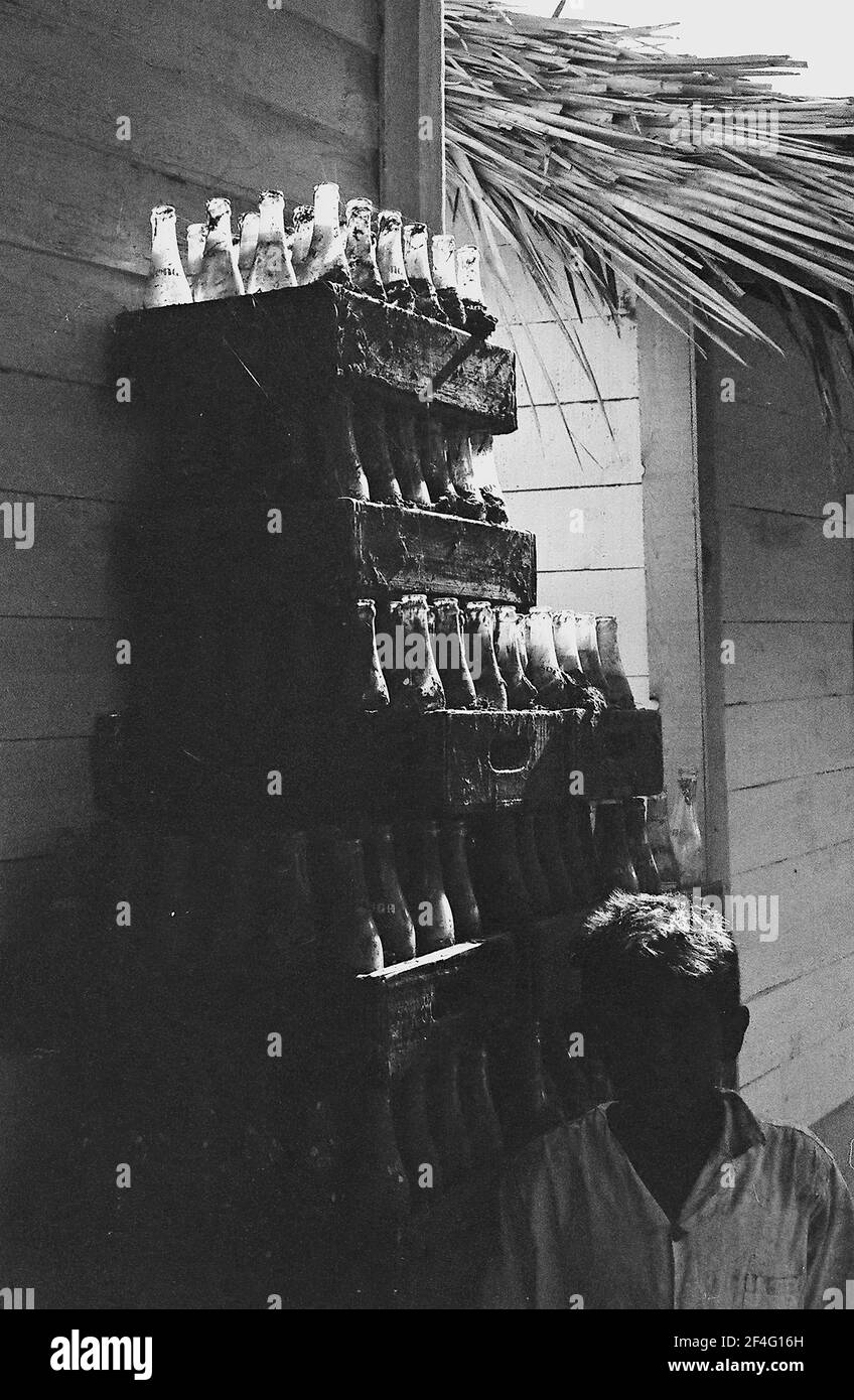 A stack of Coca Cola bottles is visible under a thatched roof with a ...