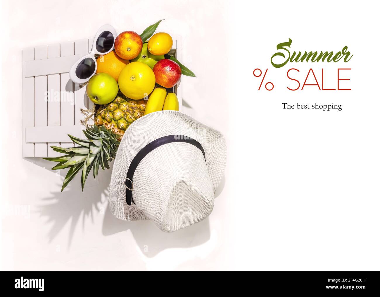 Fresh tropical fruits in a wooden box and summer hat on a white ...