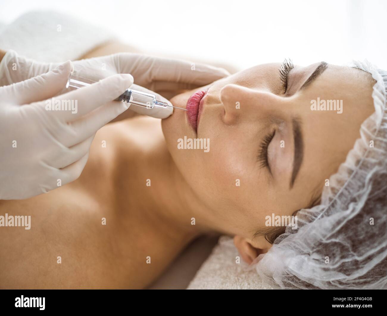 Beautician doing beauty procedure with syringe to face of young brunette woman in sunny clinic ...
