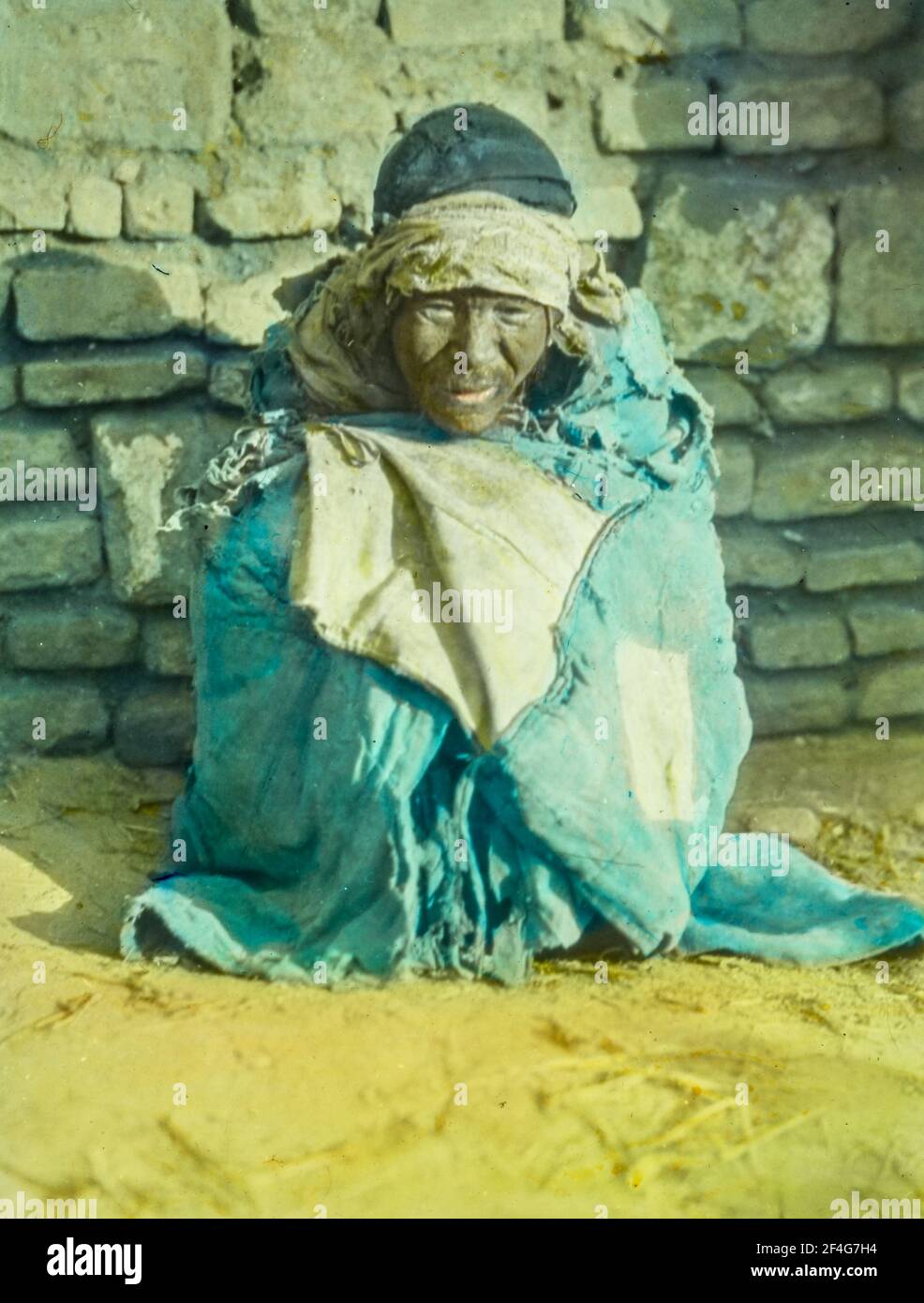 Hand-colored, Untitled lantern slide of a person kneeling in tattered ...