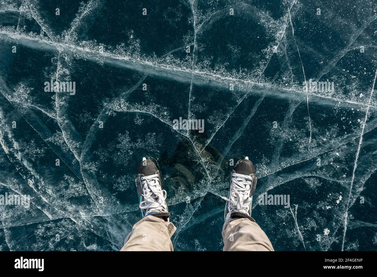 Feet in skates on the beautiful blue cracked ice of a frozen lake. Top ...