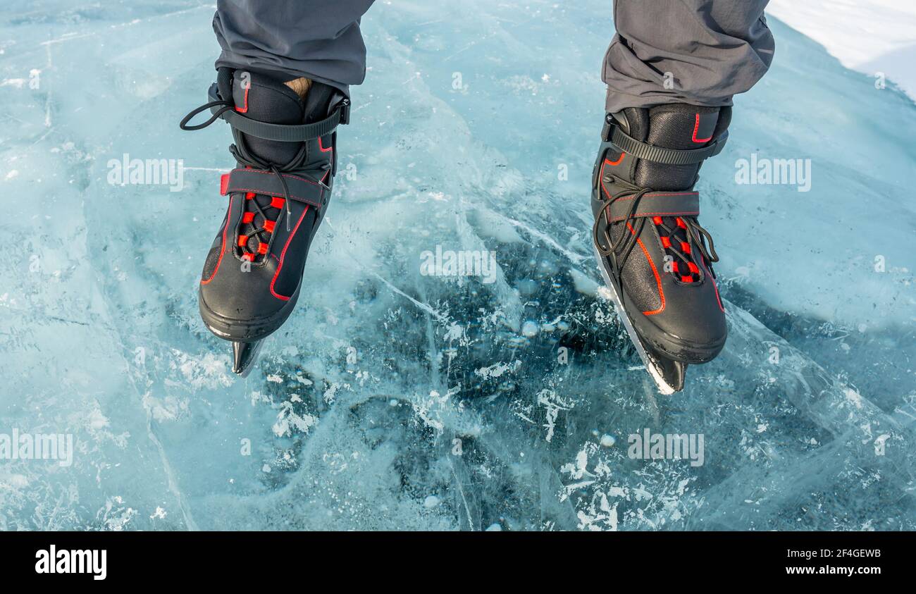 Feet in skates on the beautiful blue cracked ice of a frozen lake. Top ...