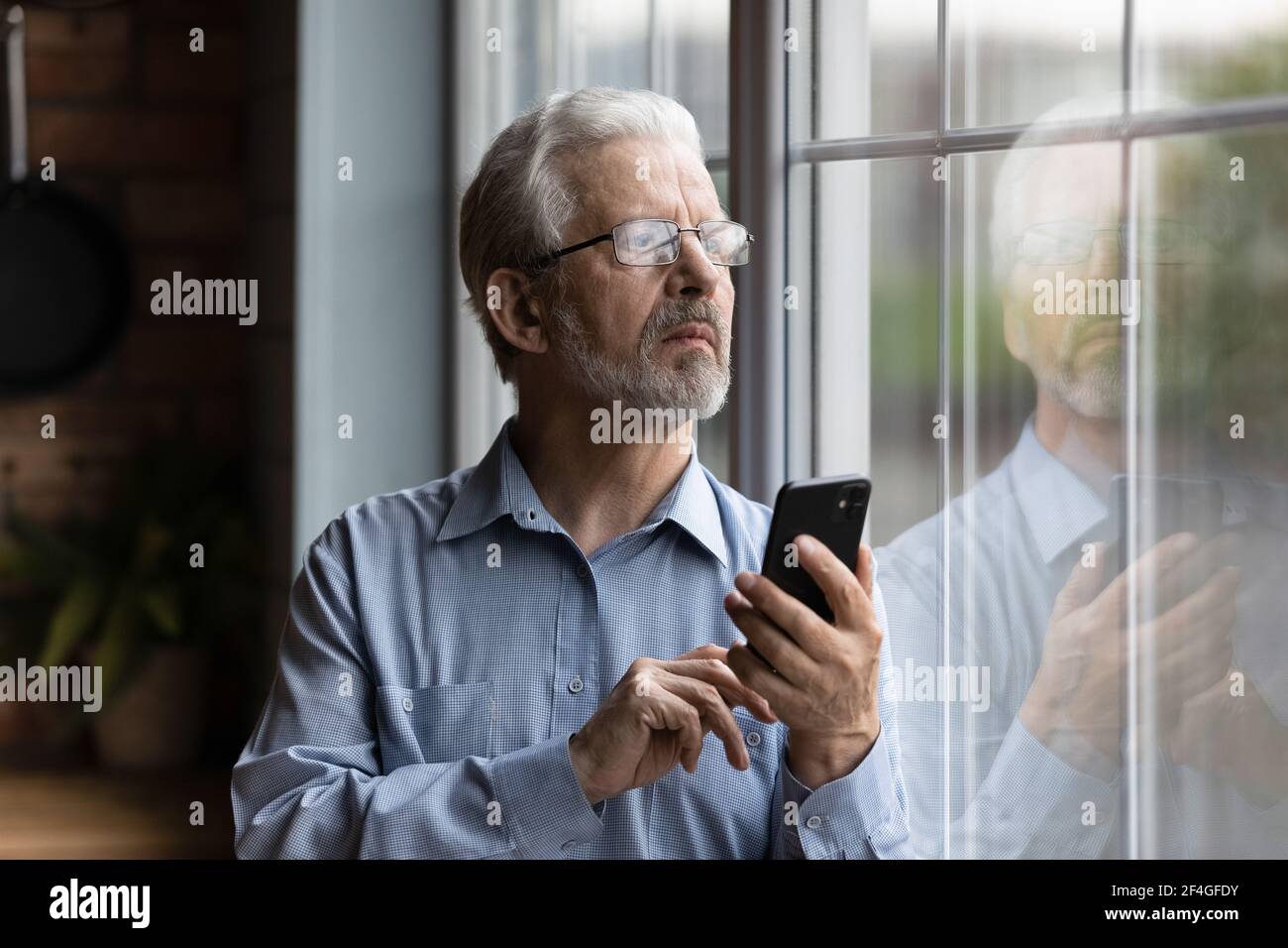 Worried older man look at window hold phone make call Stock Photo - Alamy