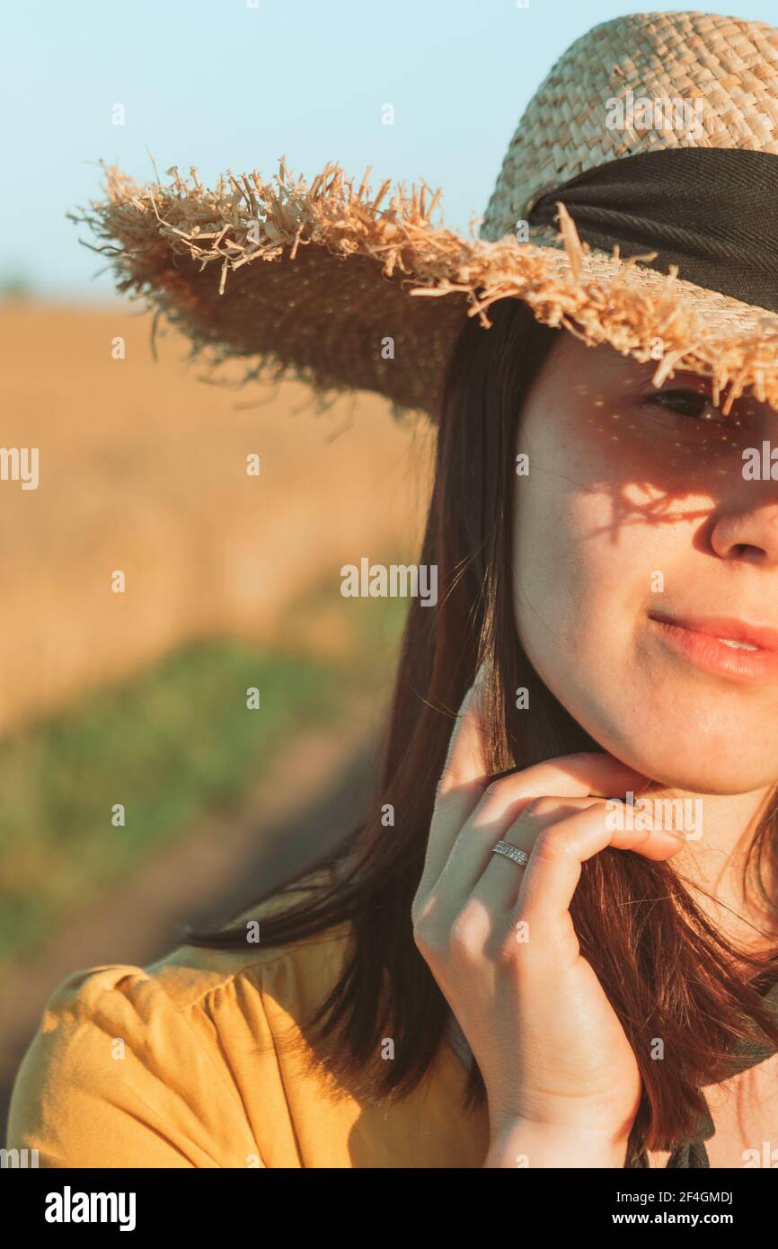 portrait of beautiful woman in straw hat on sunset in field. close up ...