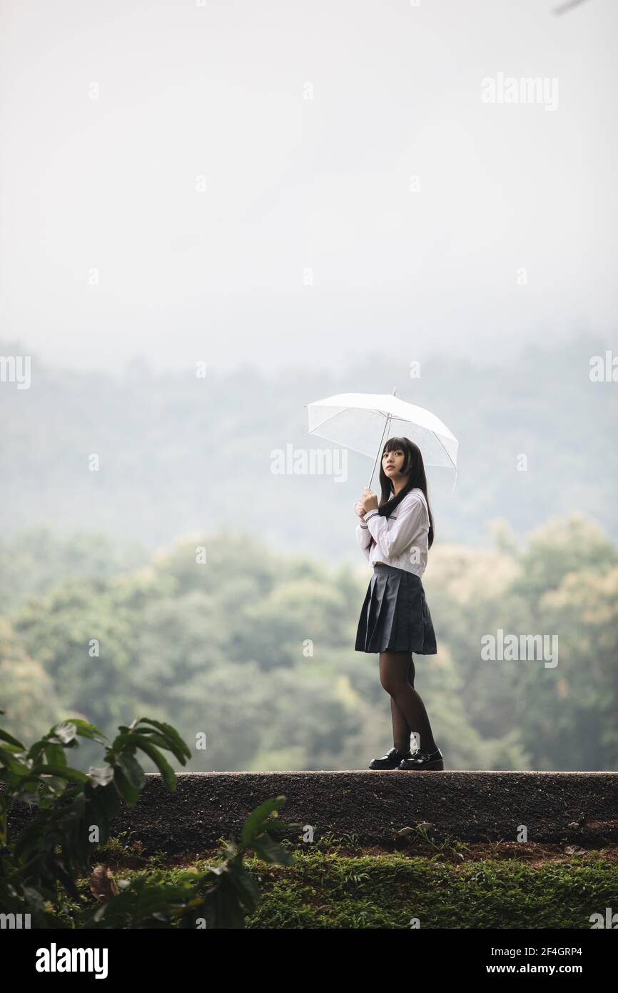 Portrait of Asian school girl walking with umbrella at nature walkway ...