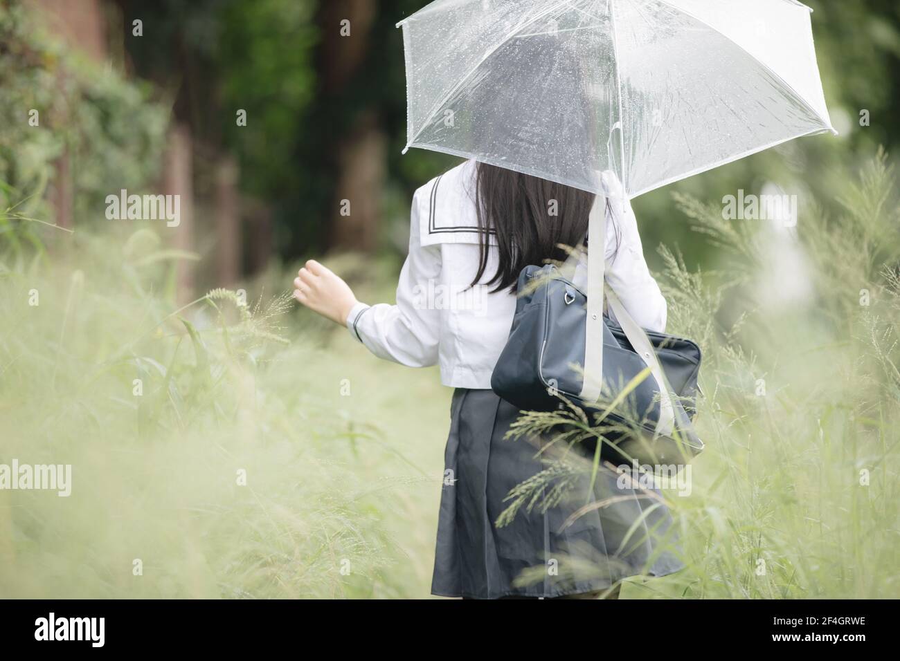 Portrait of Asian school girl walking with umbrella at nature walkway ...