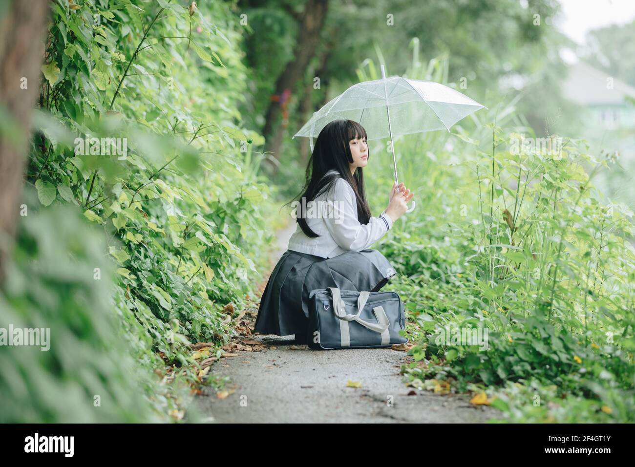 Portrait of Asian school girl walking with umbrella at nature walkway ...
