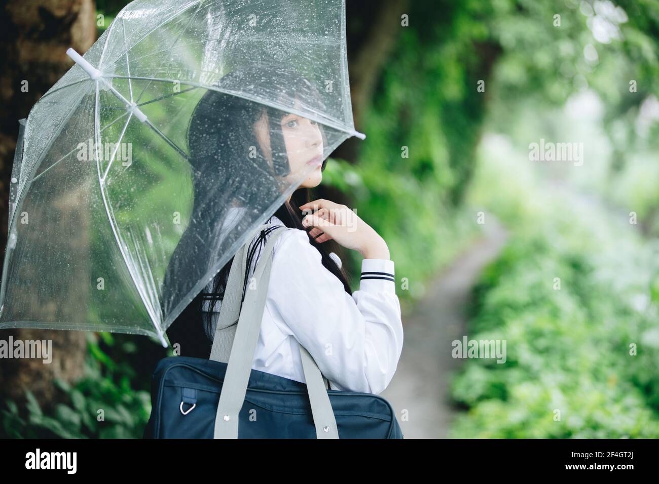 Portrait of Asian school girl walking with umbrella at nature walkway ...