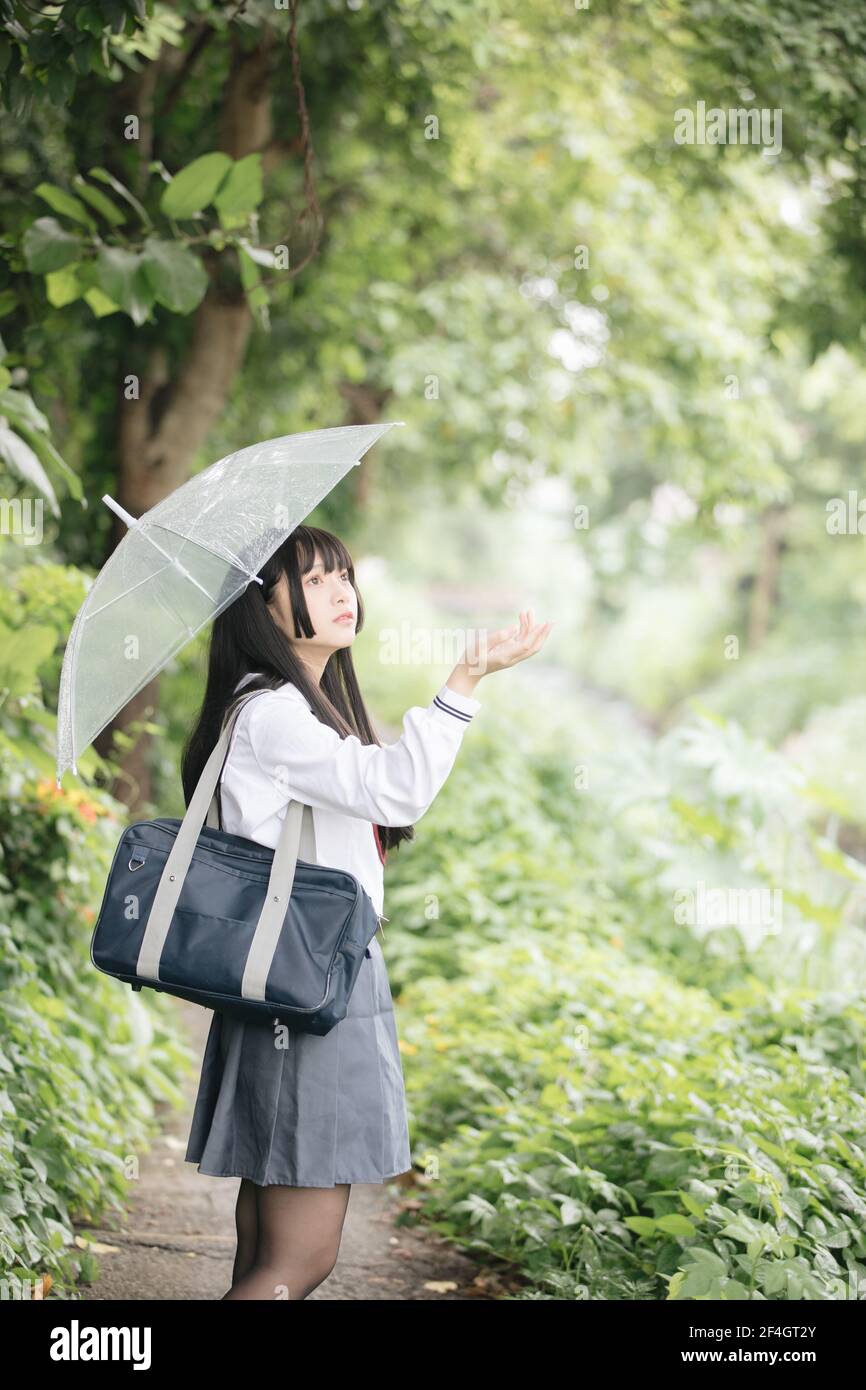 Portrait of Asian school girl walking with umbrella at nature walkway ...