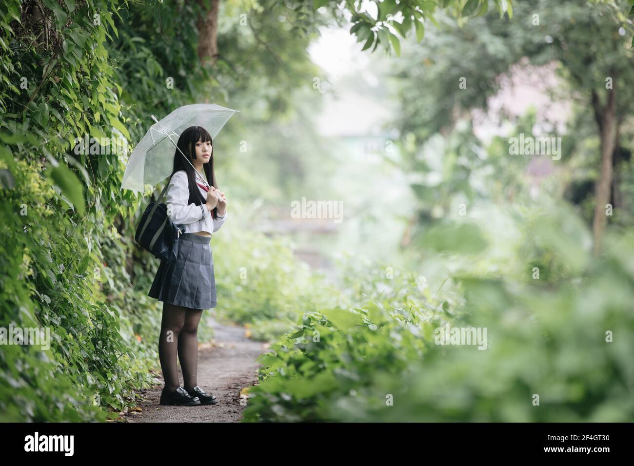 Portrait of Asian school girl walking with umbrella at nature walkway ...