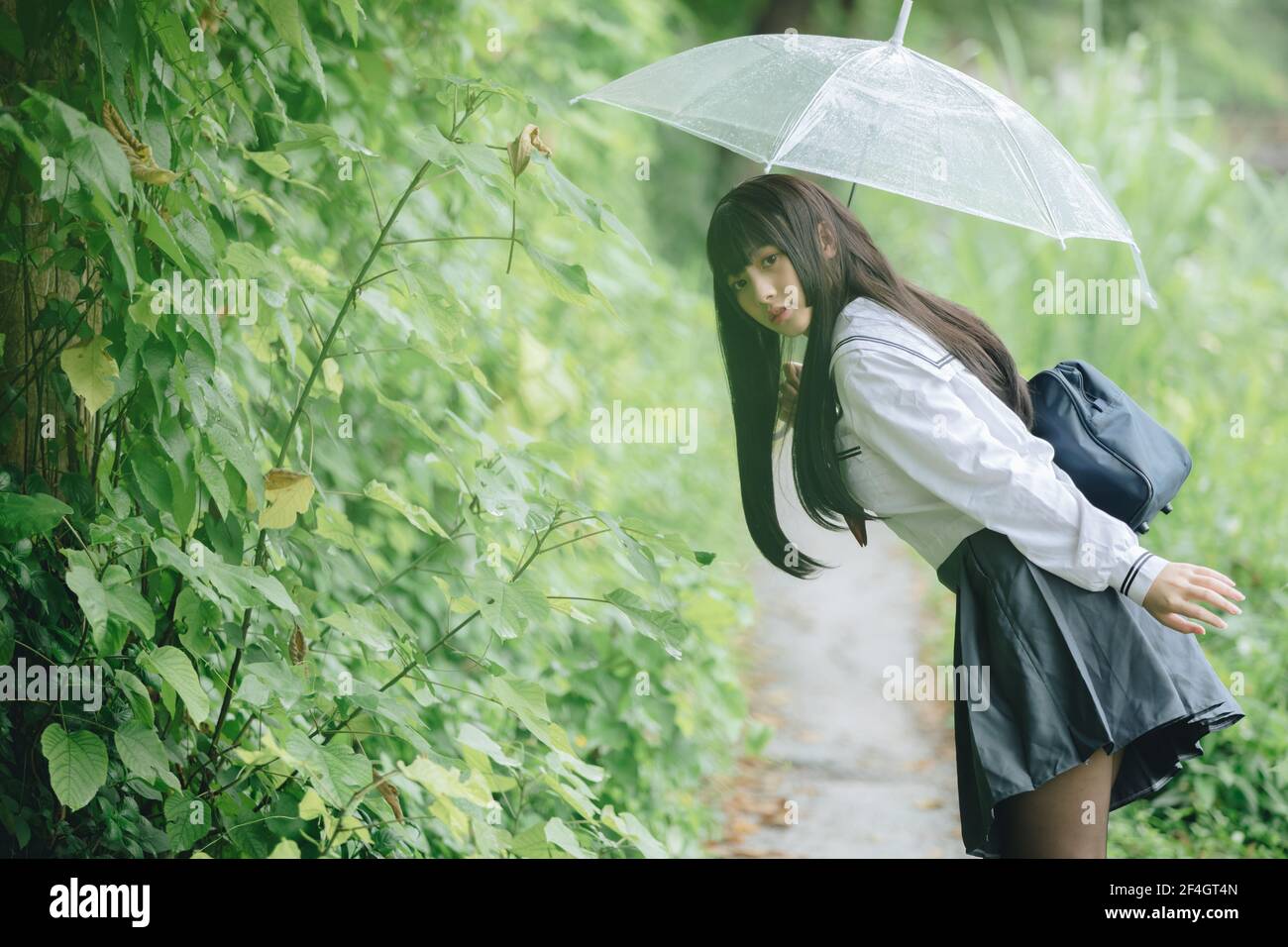 Portrait of Asian school girl walking with umbrella at nature walkway ...