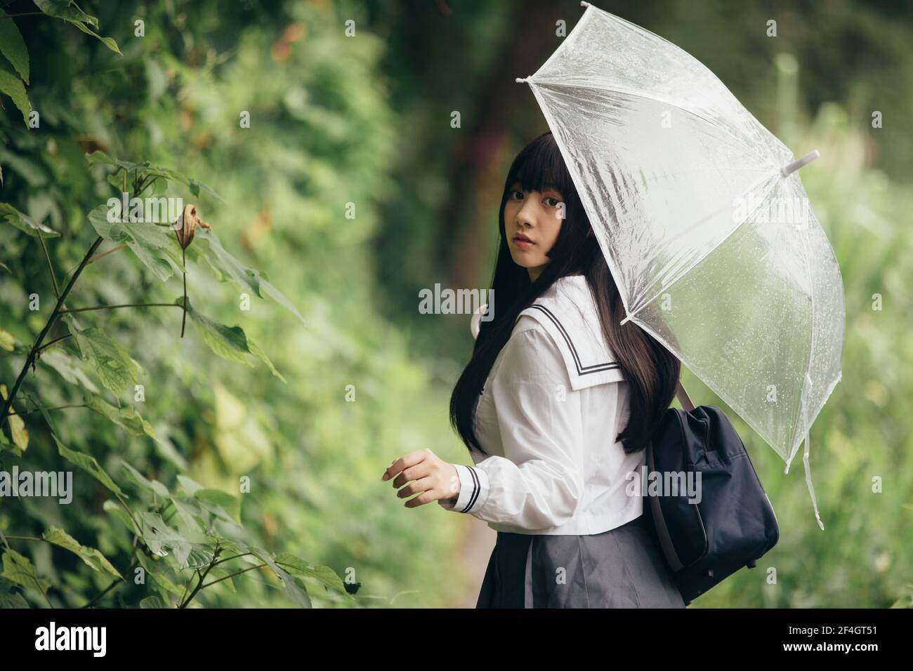 Portrait of Asian school girl walking with umbrella at nature walkway ...