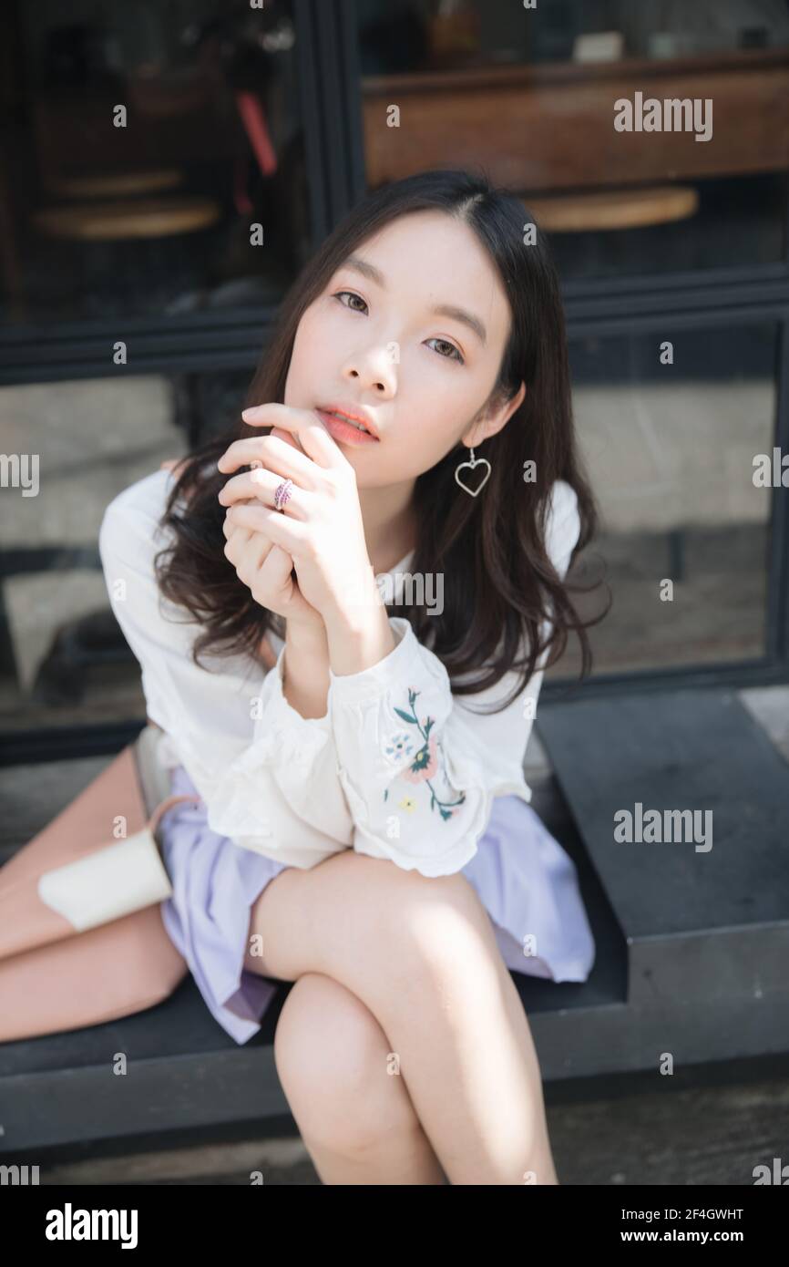 portrait of asian girl with white shirt and skirt sitting and looking ...