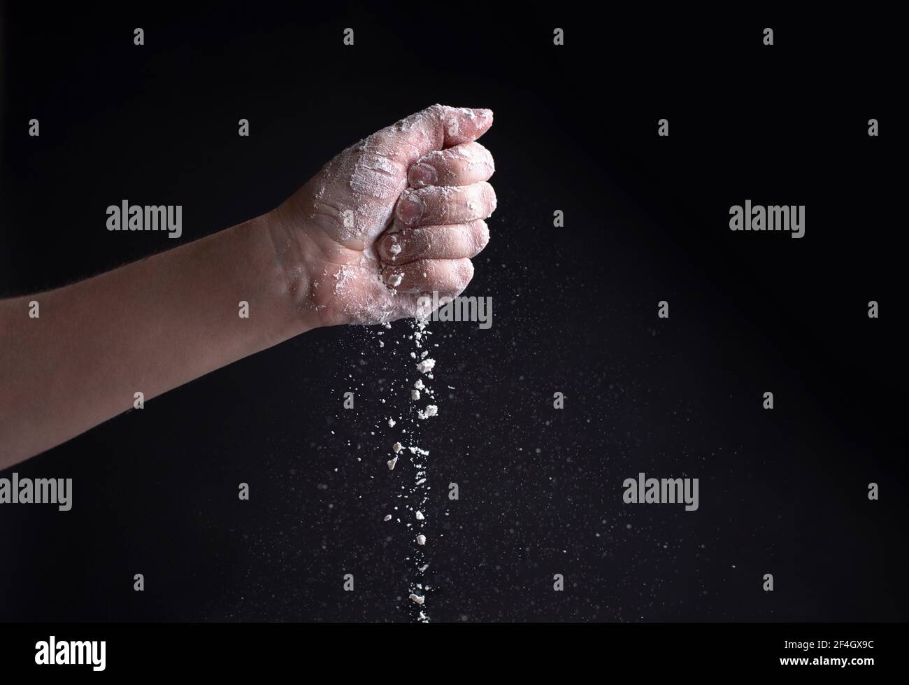 Female hand pouring flour on a black background, flying white powder ...