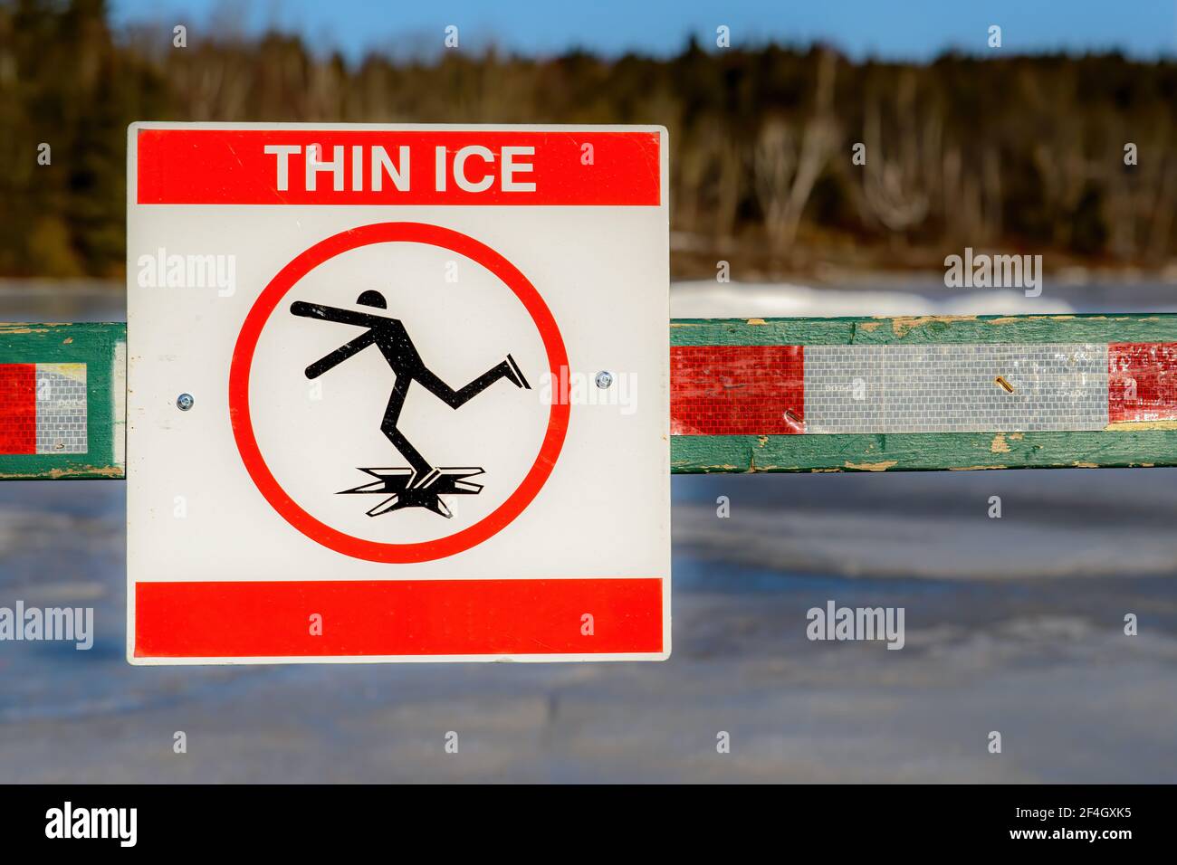 A sign by a frozen lake warning of thin ice. It is mounted on an old ...
