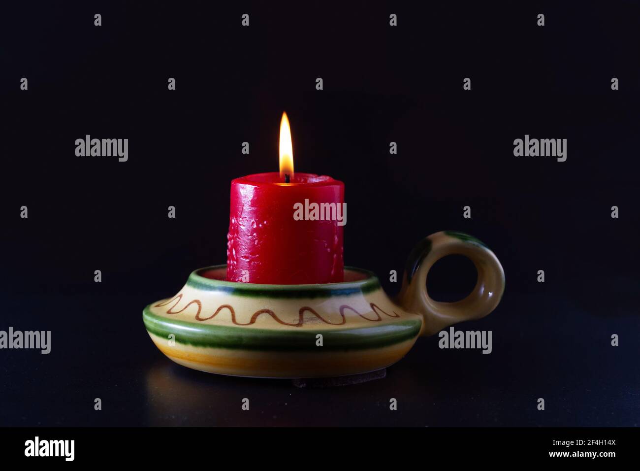A lit red candle in a yellow and green ceramic candlestick. Cocept of ...