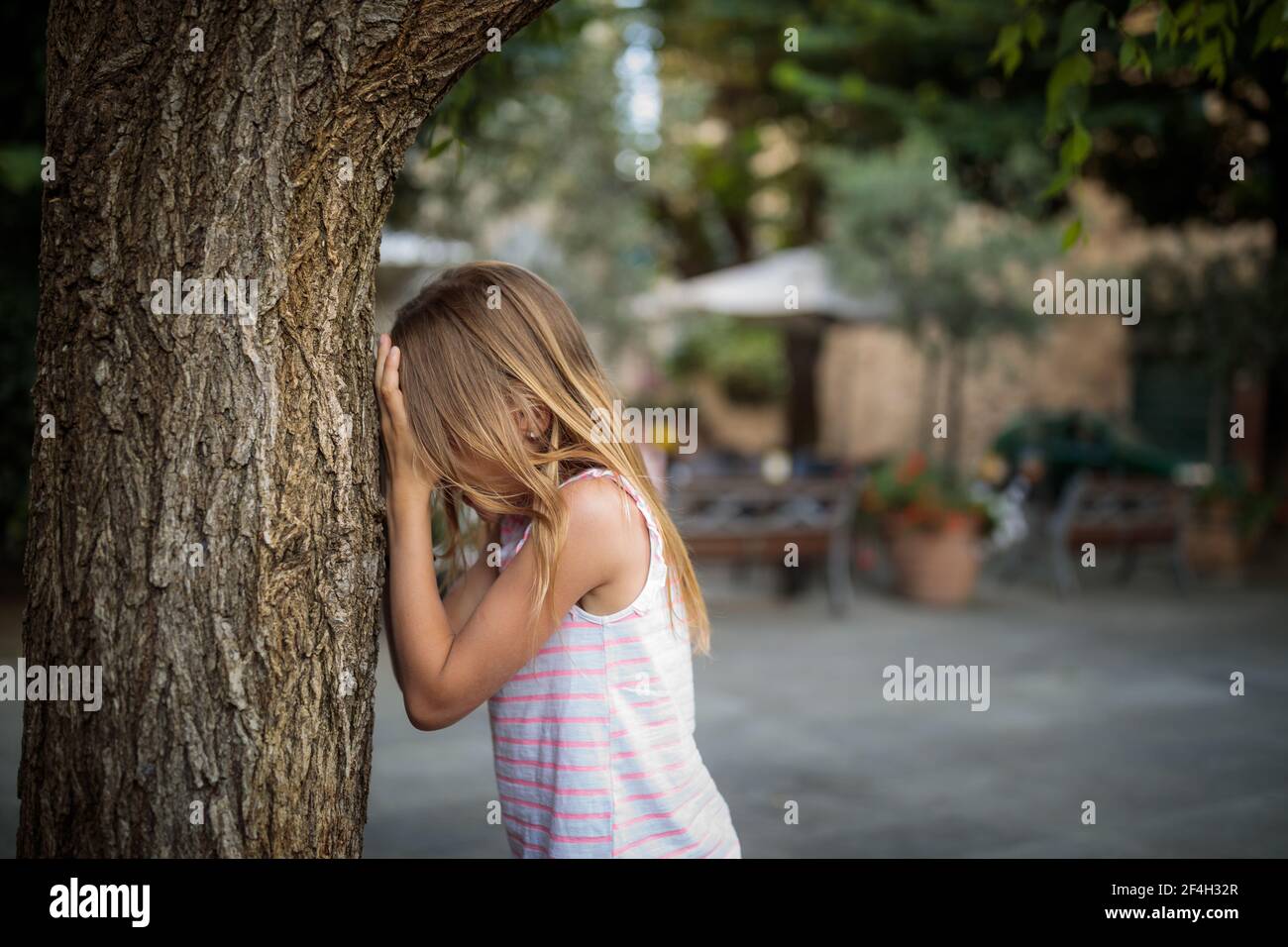 Little girl playing hide and seek with friends, counting by a tree, waiting for them to hide ...