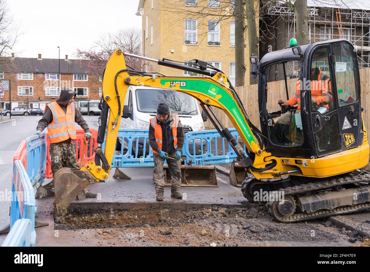 three man working with JCB digger dig up a hole in road for sewage pipe ...
